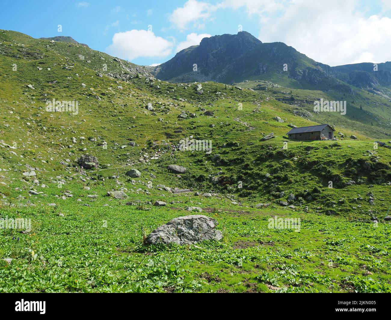 A green landscape with a small house surrounded by rocky mountains in ...