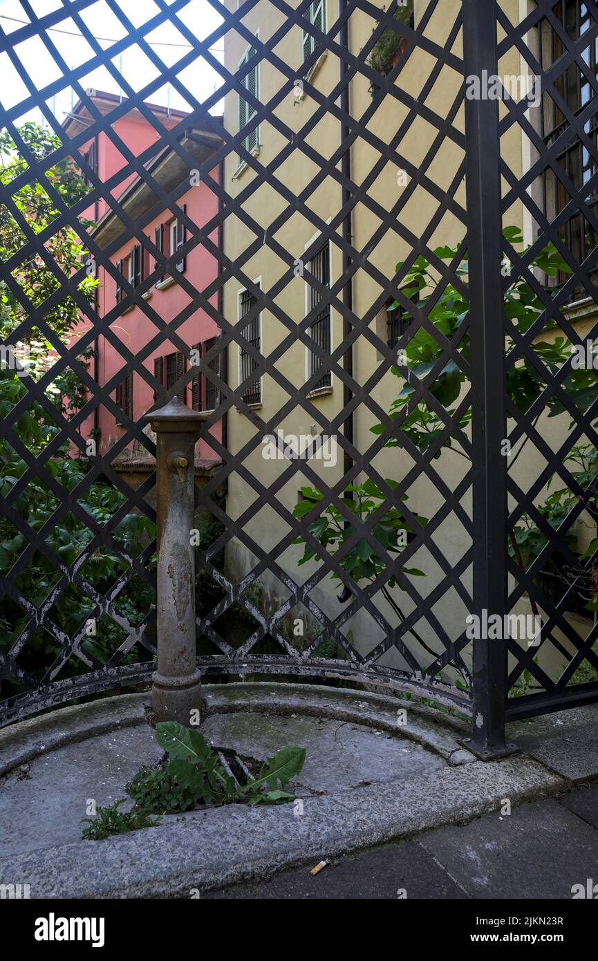 Old public fountain in front of a fence with a row of houses and a fig ...