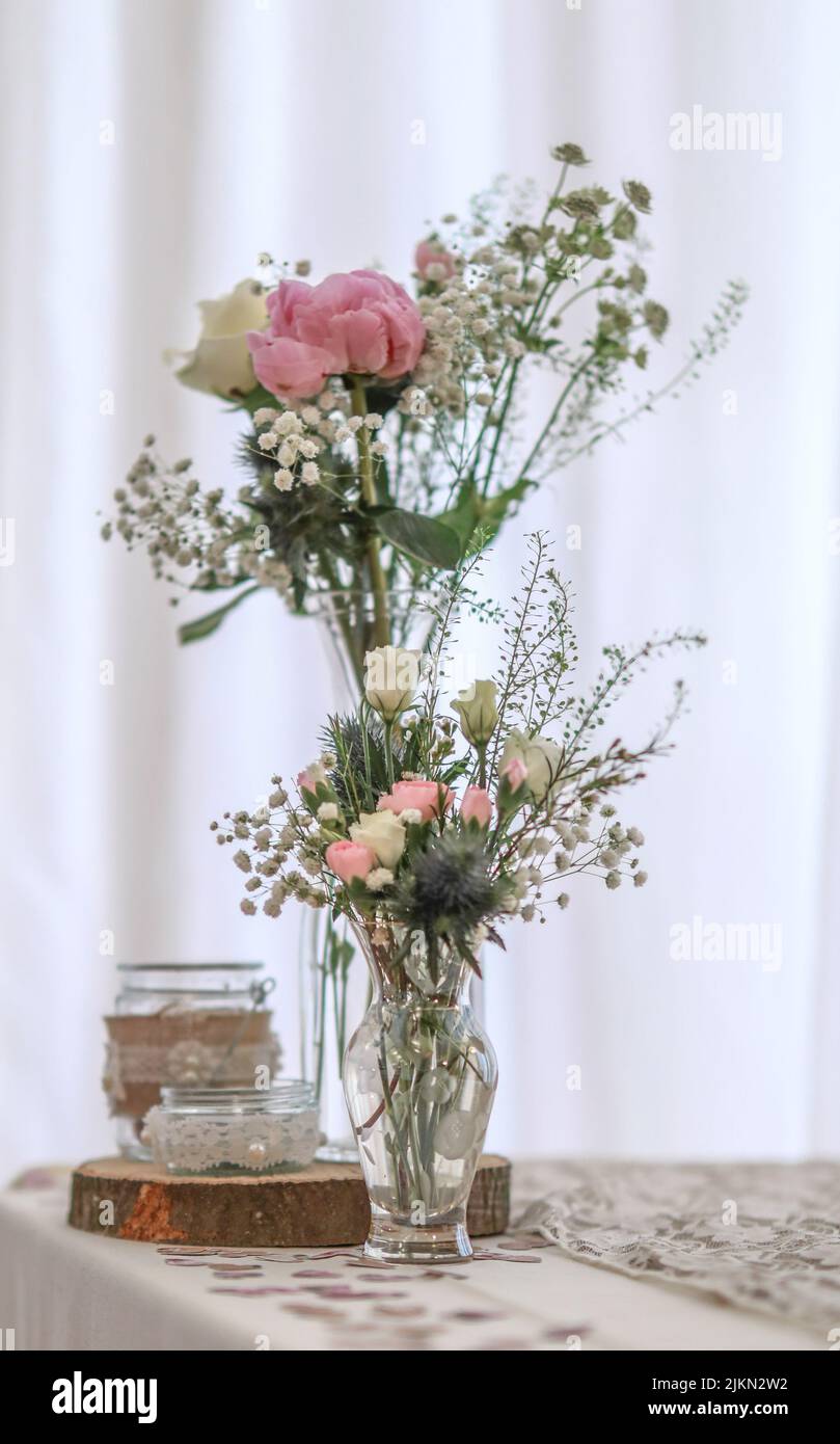 A vertical shot of glass vase with white and pink roses on table in ...