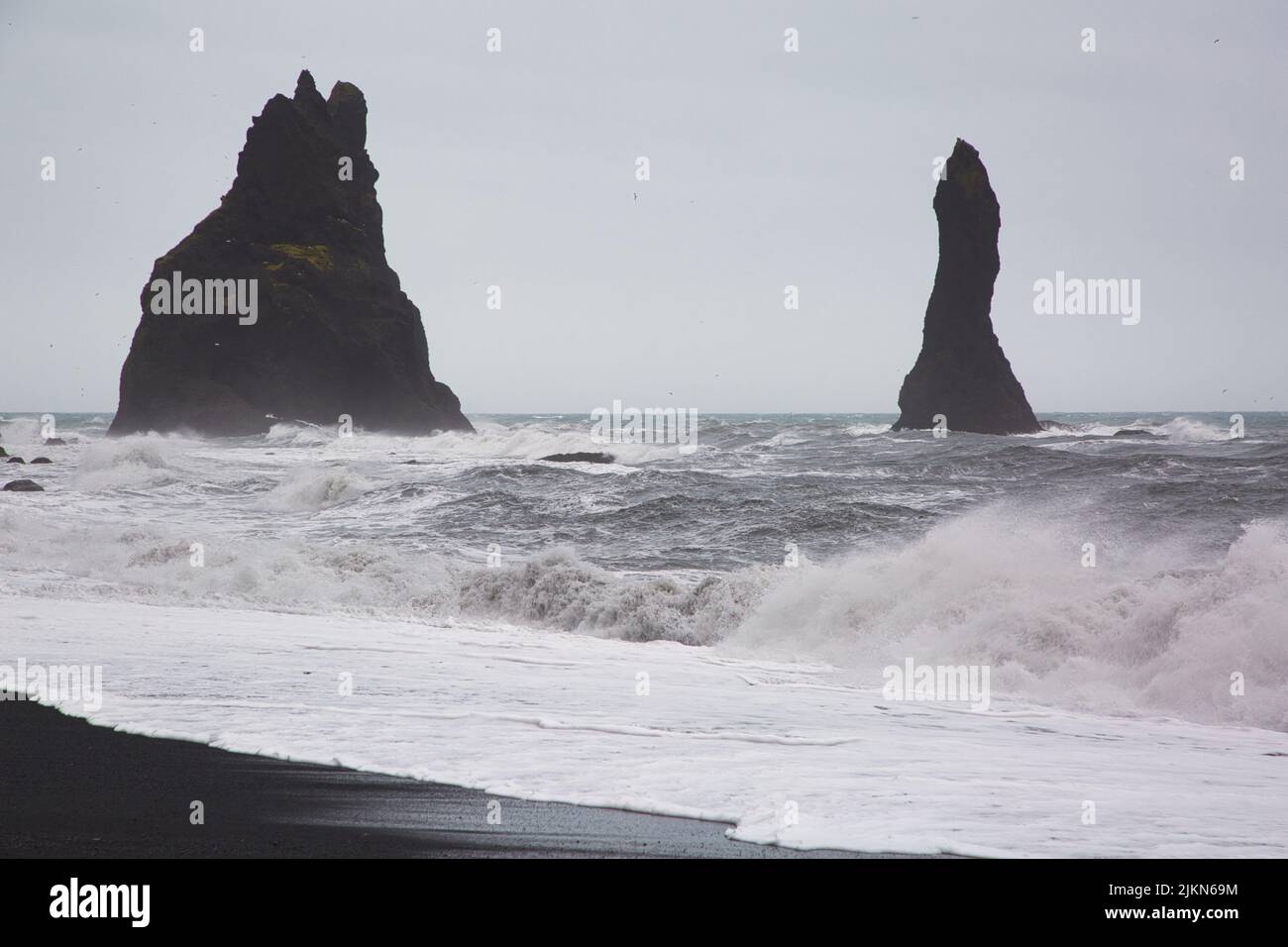 Two sea stacks stand against the waves on the Reynisdrangar, Iceland ...