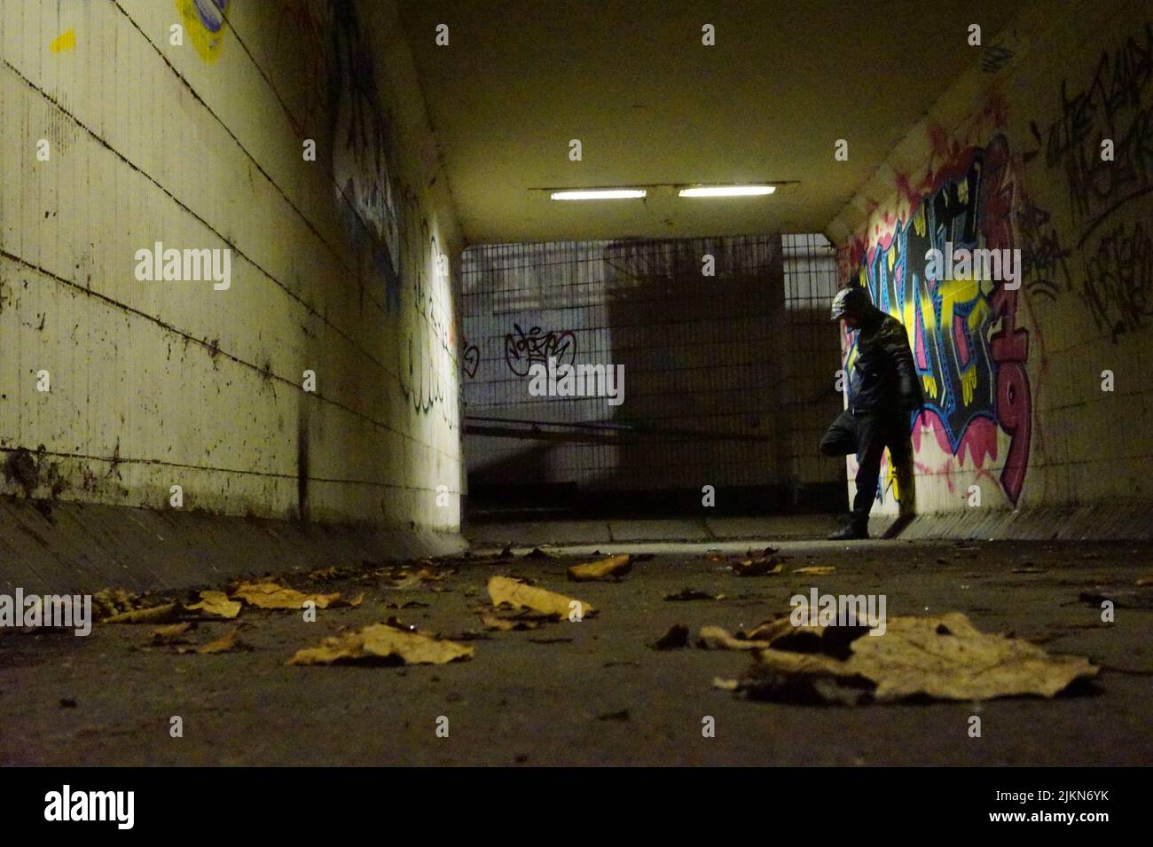 A side profile view of a young man leaning against a wall, dirty subway ...