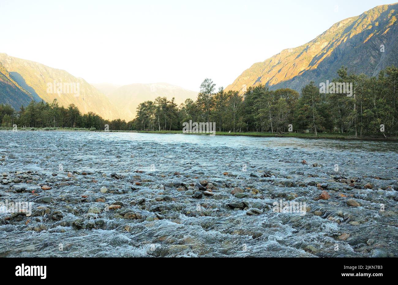 View from the water's edge of a shallow river with rocky banks flowing ...