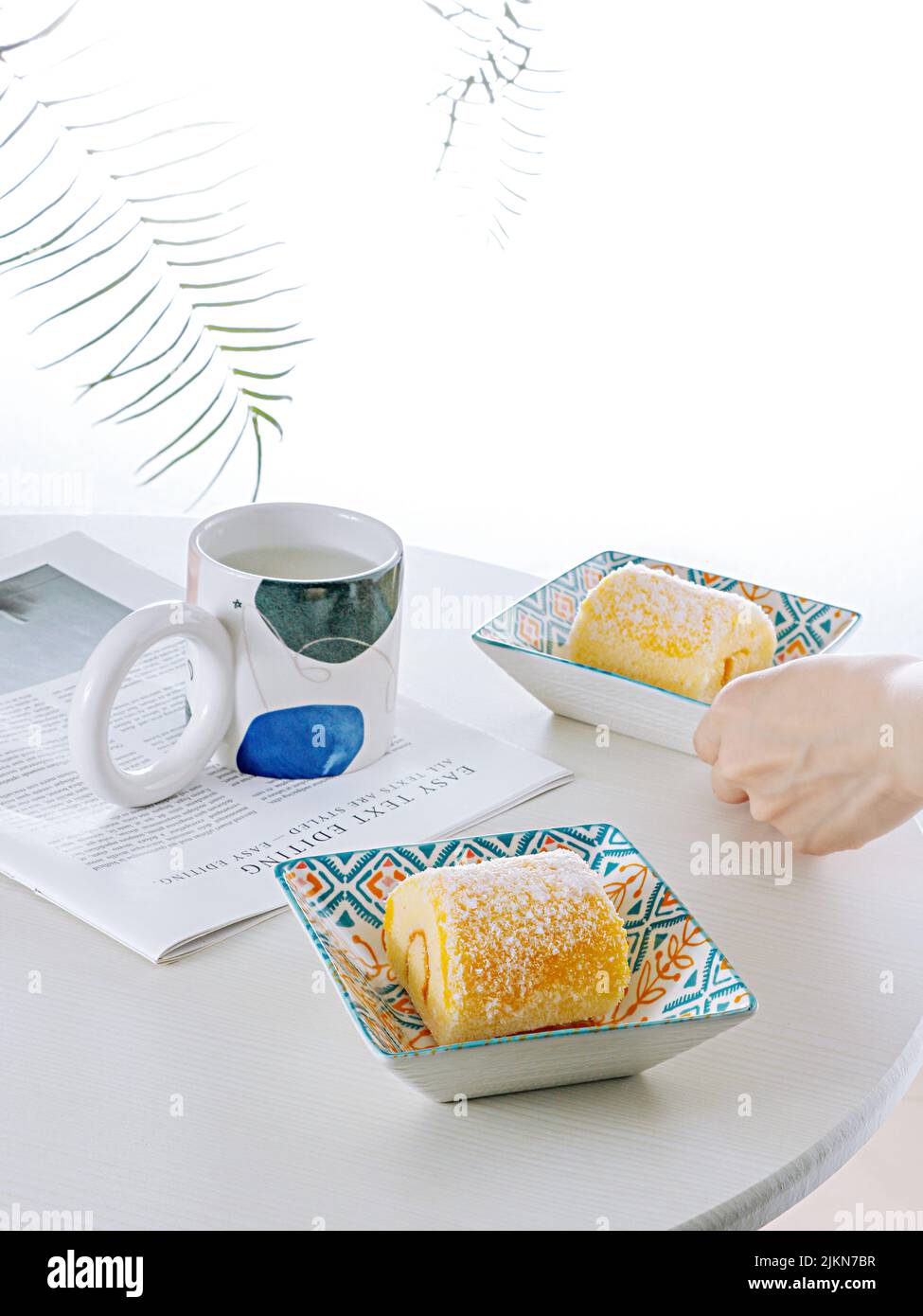 A vertical shot of a person eating swiss roll dessert and drinking tea ...
