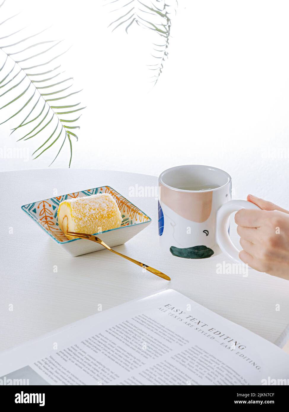 A vertical shot of a person eating swiss roll dessert and drinking tea ...