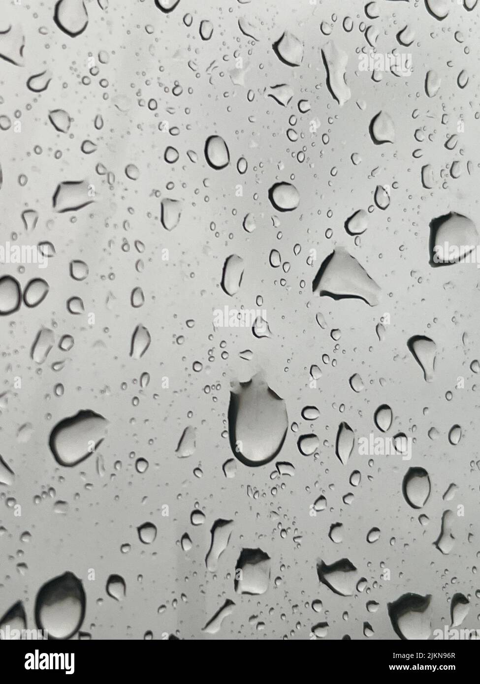 A vertical shot of raindrops running down a window on a grey background ...