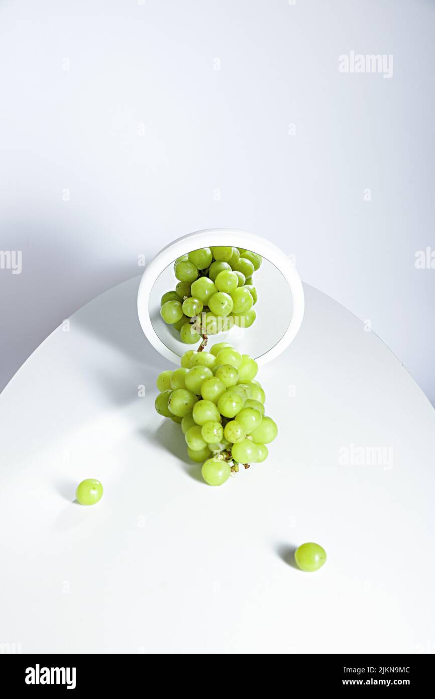 A vertical shot of white grape reflecting on the round mirror on a ...