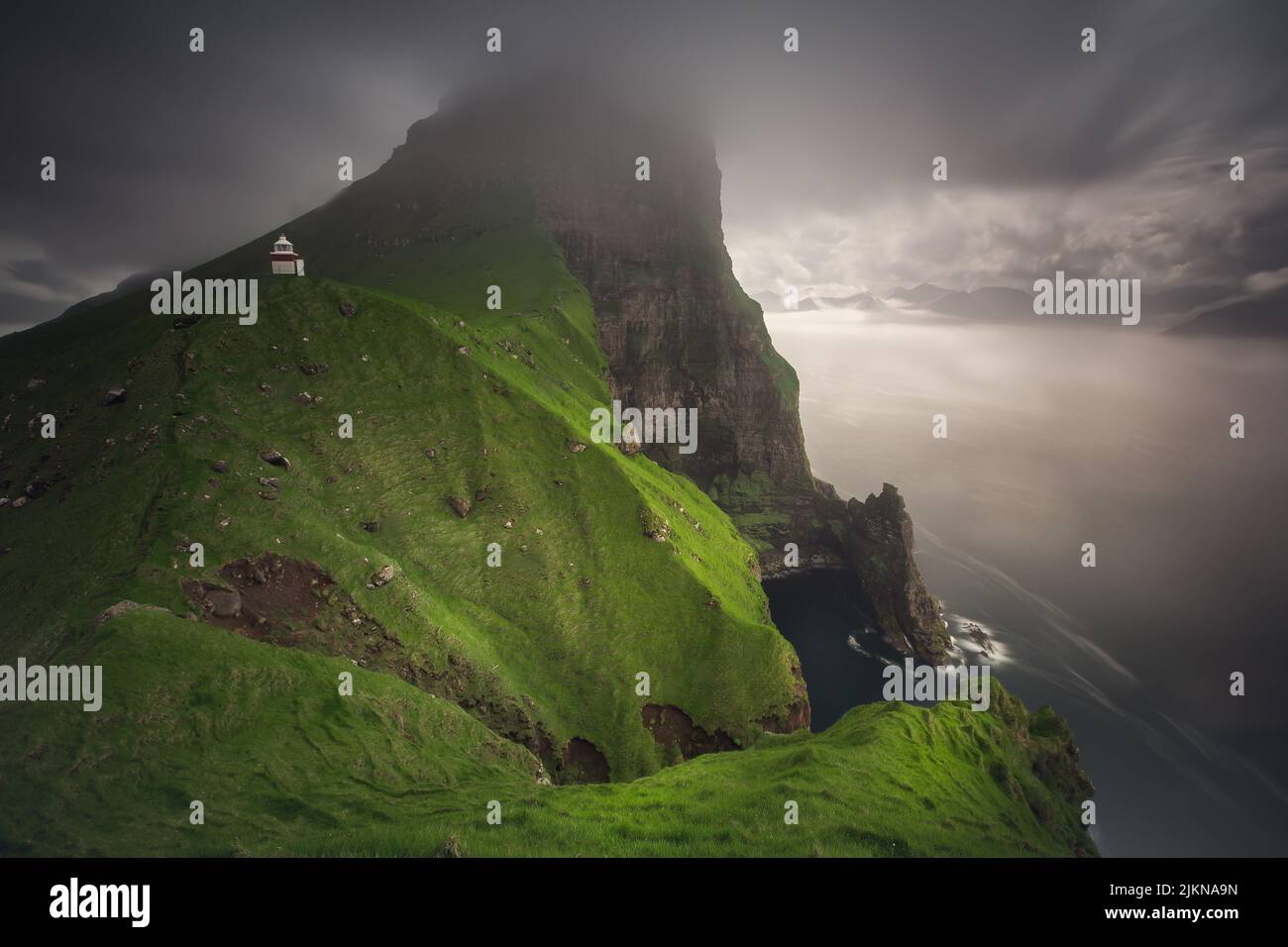 A giant, green rocky cliff with its peak shrouded in gray clouds ...