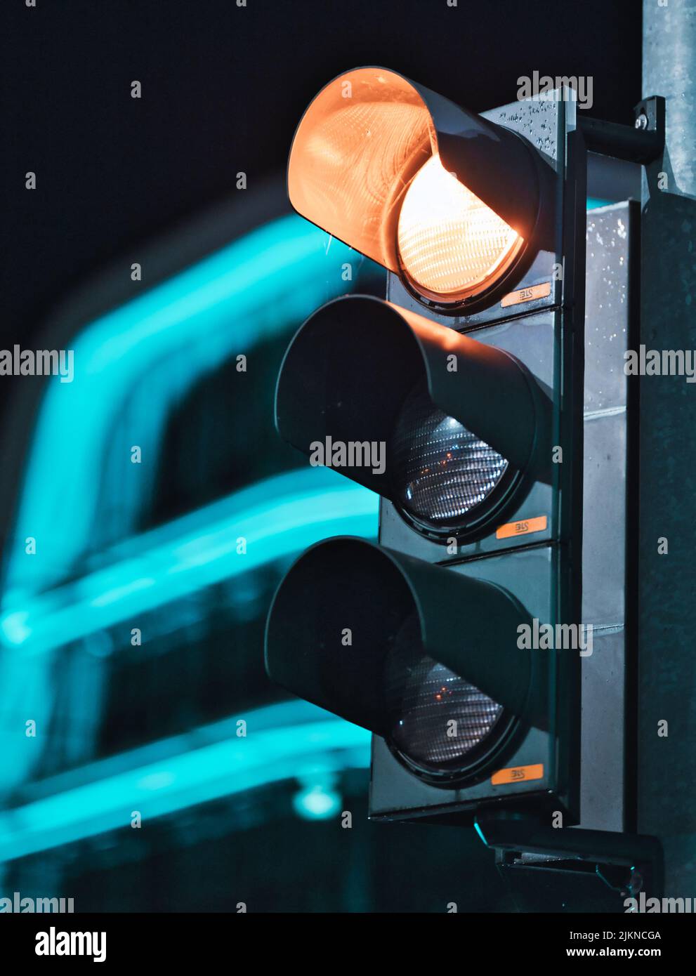 A vertical closeup of the orange light on the traffic lights at night ...