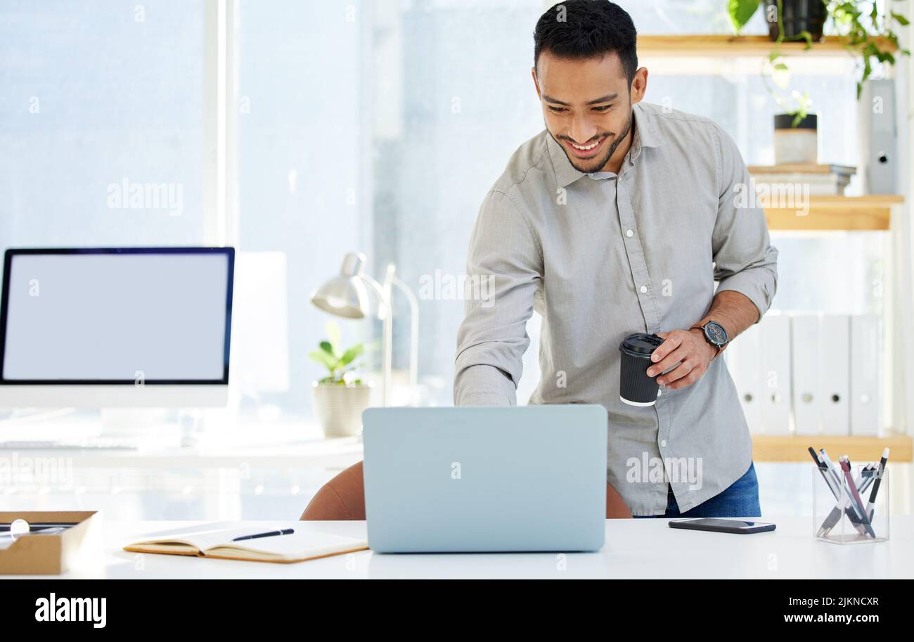 Getting some funny emails from my coworkers. a young man using his laptop at work in a modern ...