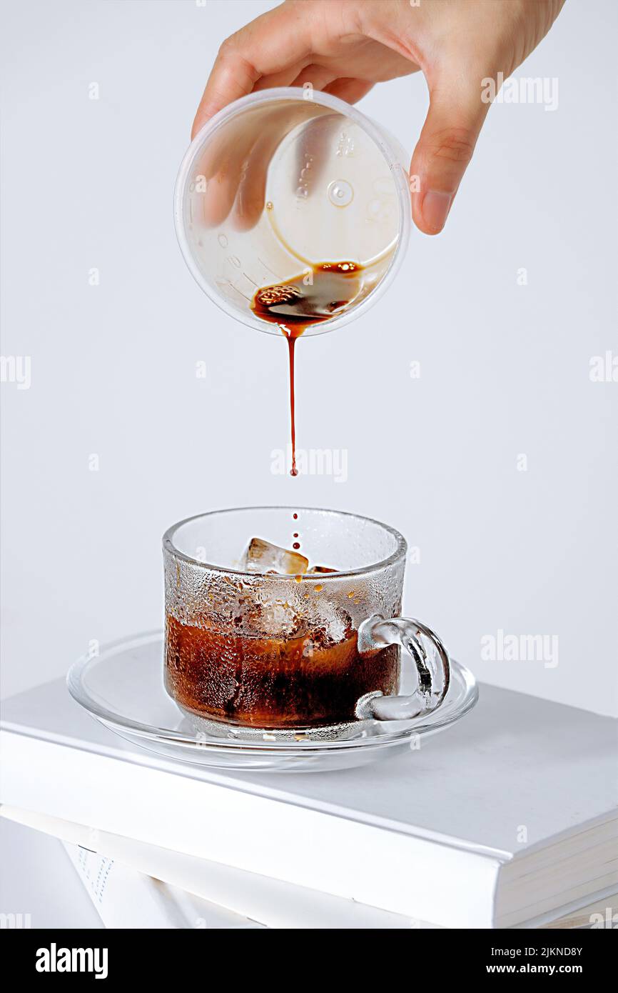 A vertical shot of a hand gradually adding coffee to a cup with ice ...