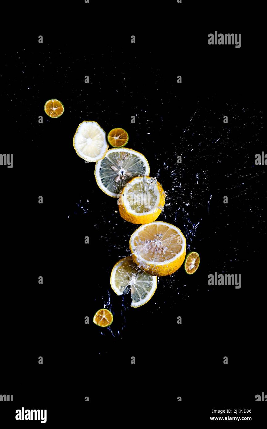 Many lemon and lime slices splashing and floating on a black background ...