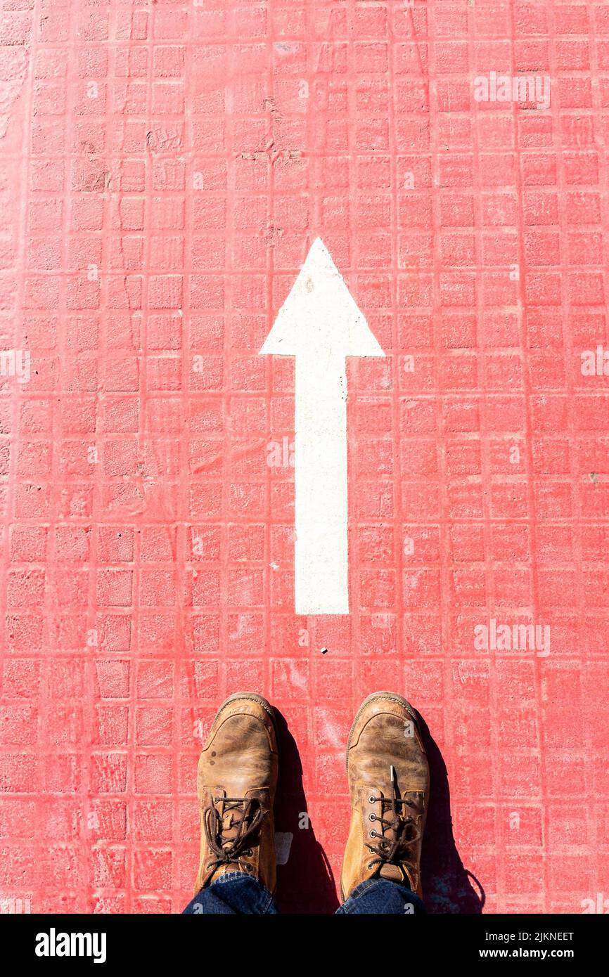 A vertical photo of man's feet on a red cycle path with an arrow sign ...