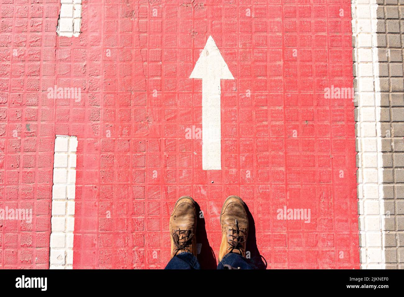 A photo of man's feet on a red cycle path with an arrow sign Stock ...