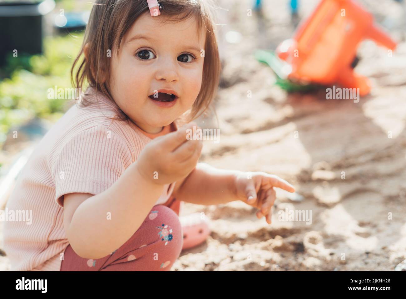 Baby girl playing in the sand in the garden showing the camera what she ...