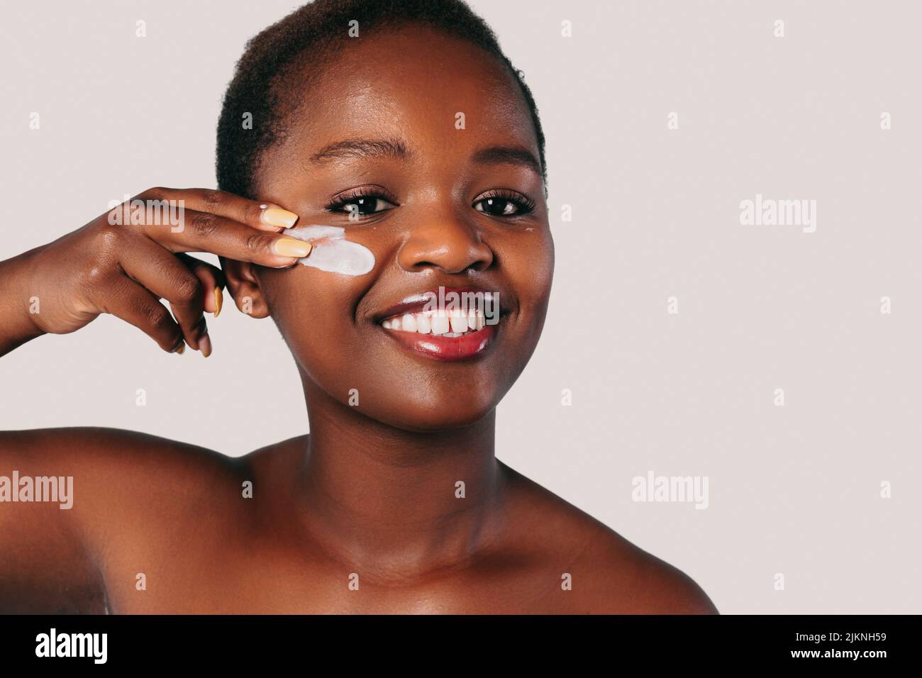 African american woman applying cream on her cheek, standing over white ...