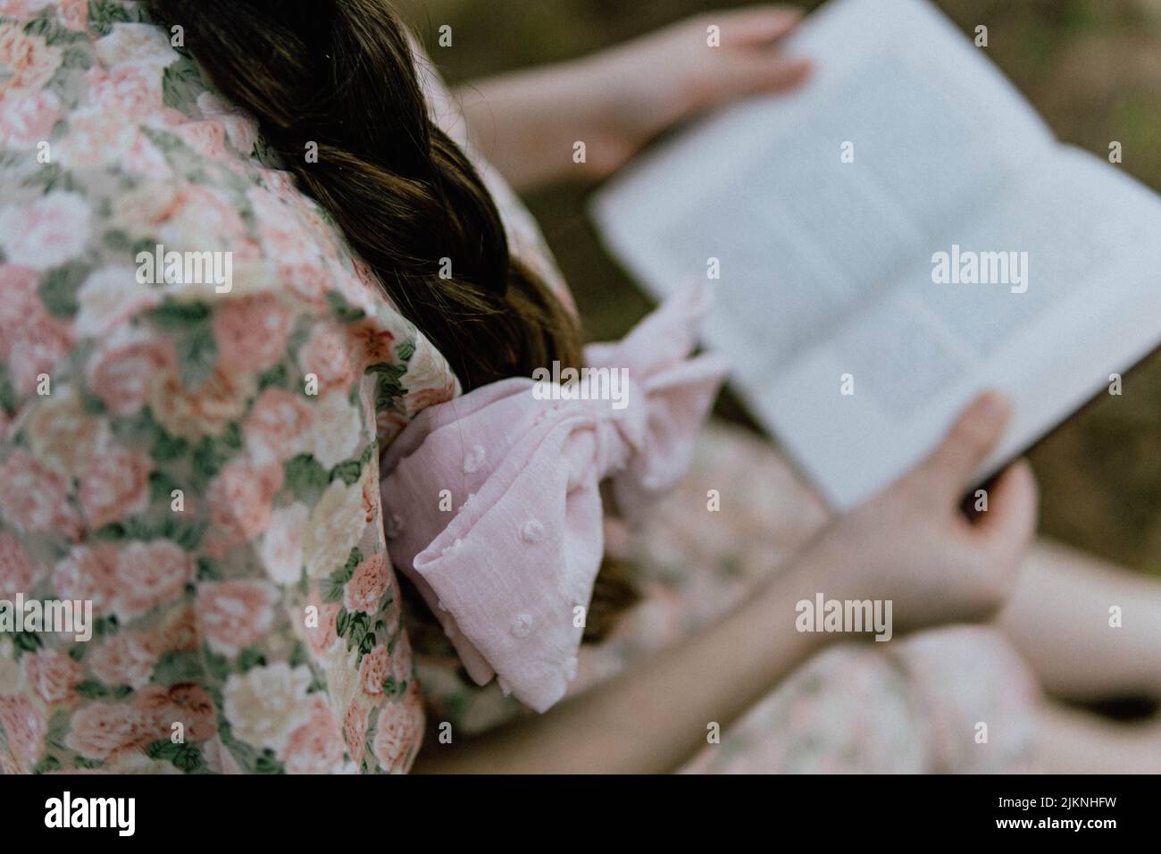 A female in a floral dress and braided hair reading a book Stock Photo ...