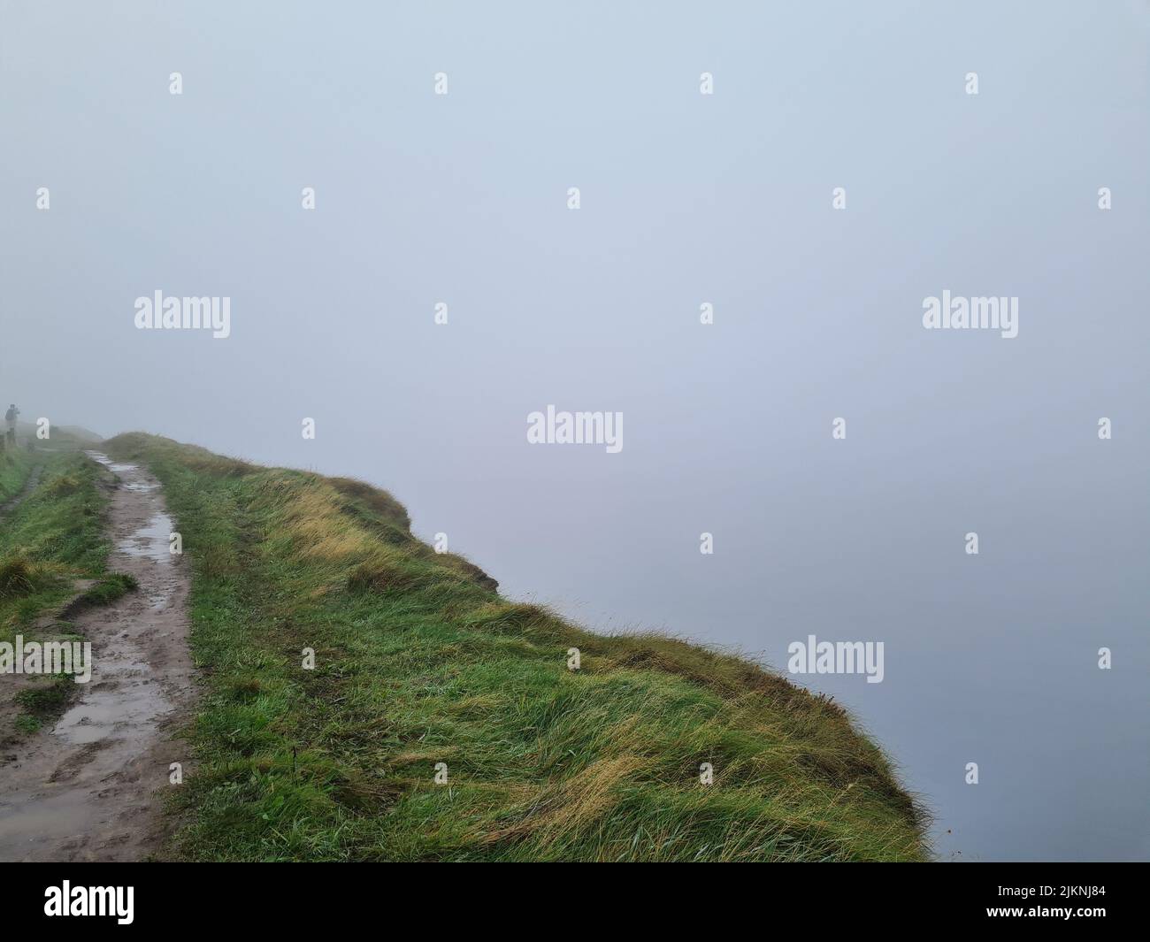 The narrow muddy trail surrounded by green grass against the gray ...