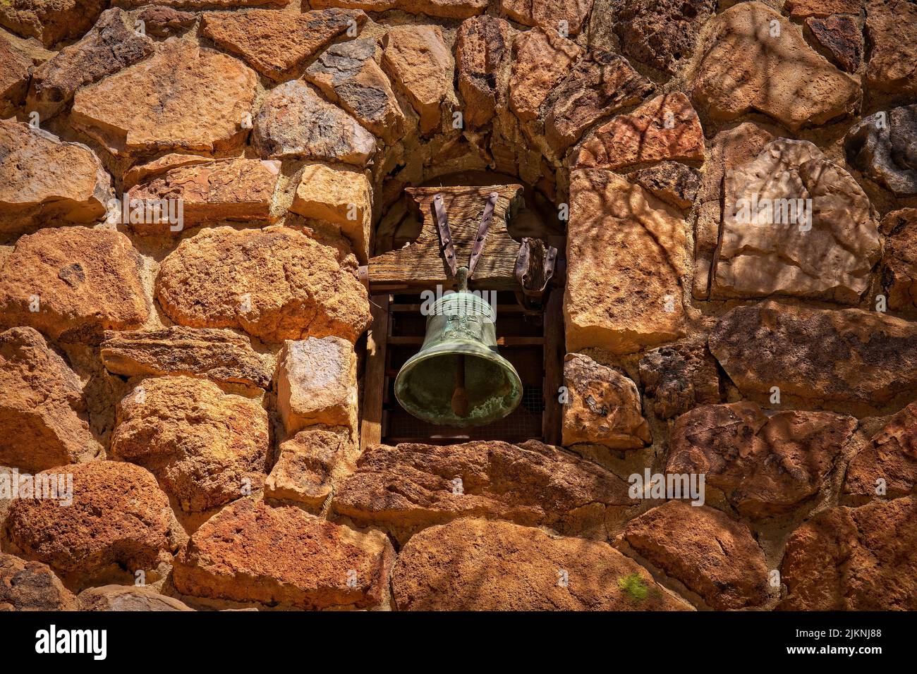An old mission bell, covered in green patina, hangs in a rough rock ...