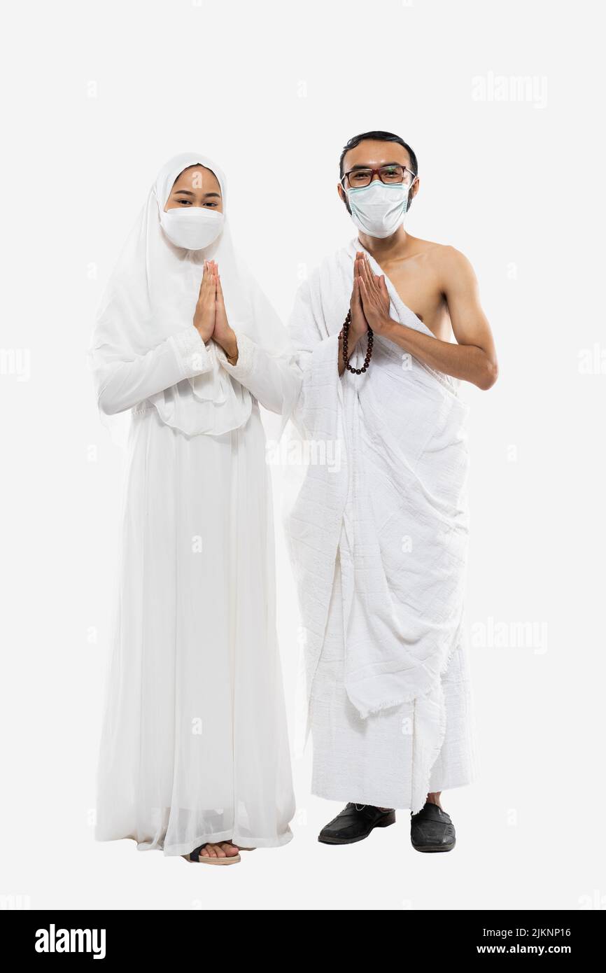 Couple wearing hajj ihram clothes and masks with greeting gesture Stock ...