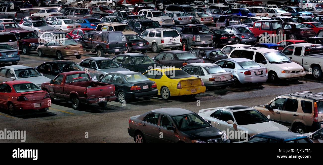 A high angle shot of a parking lot full of cars lit by streetlights ...
