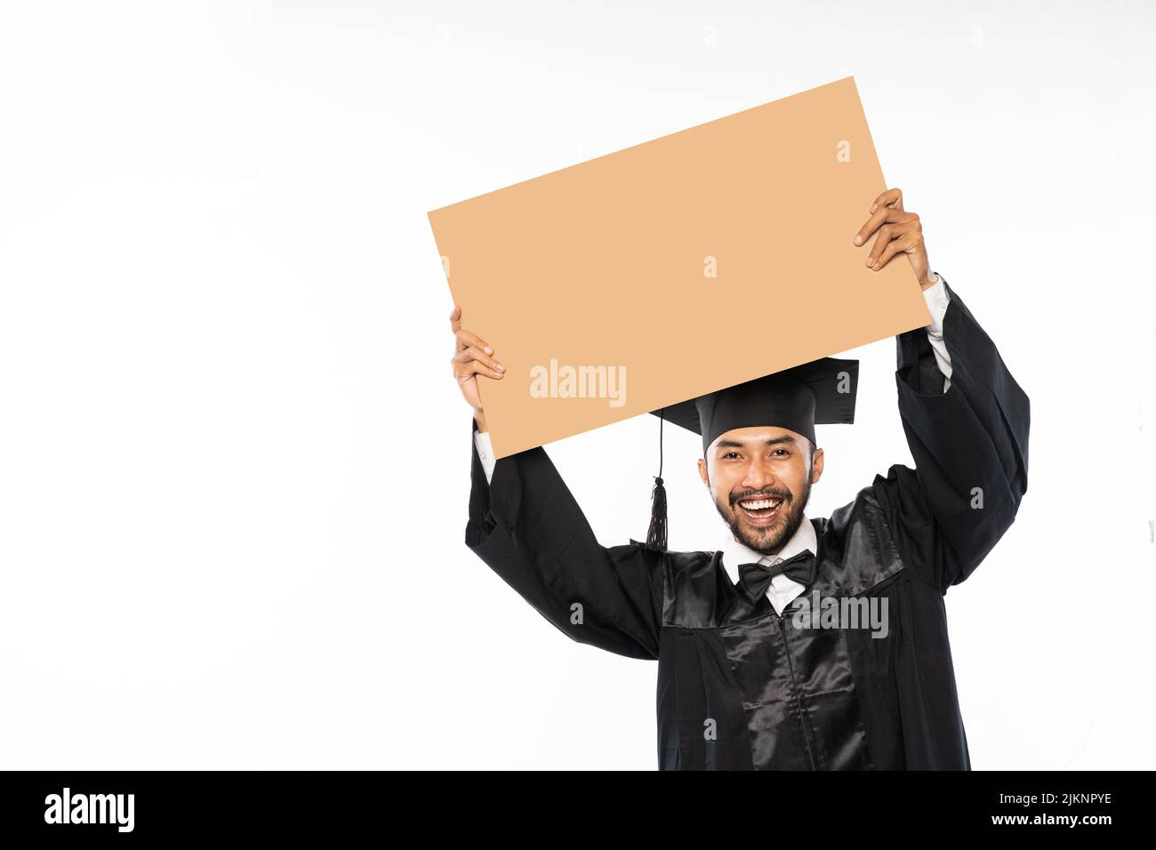 Laughing male graduate student wearing toga holding cardboard blank ...