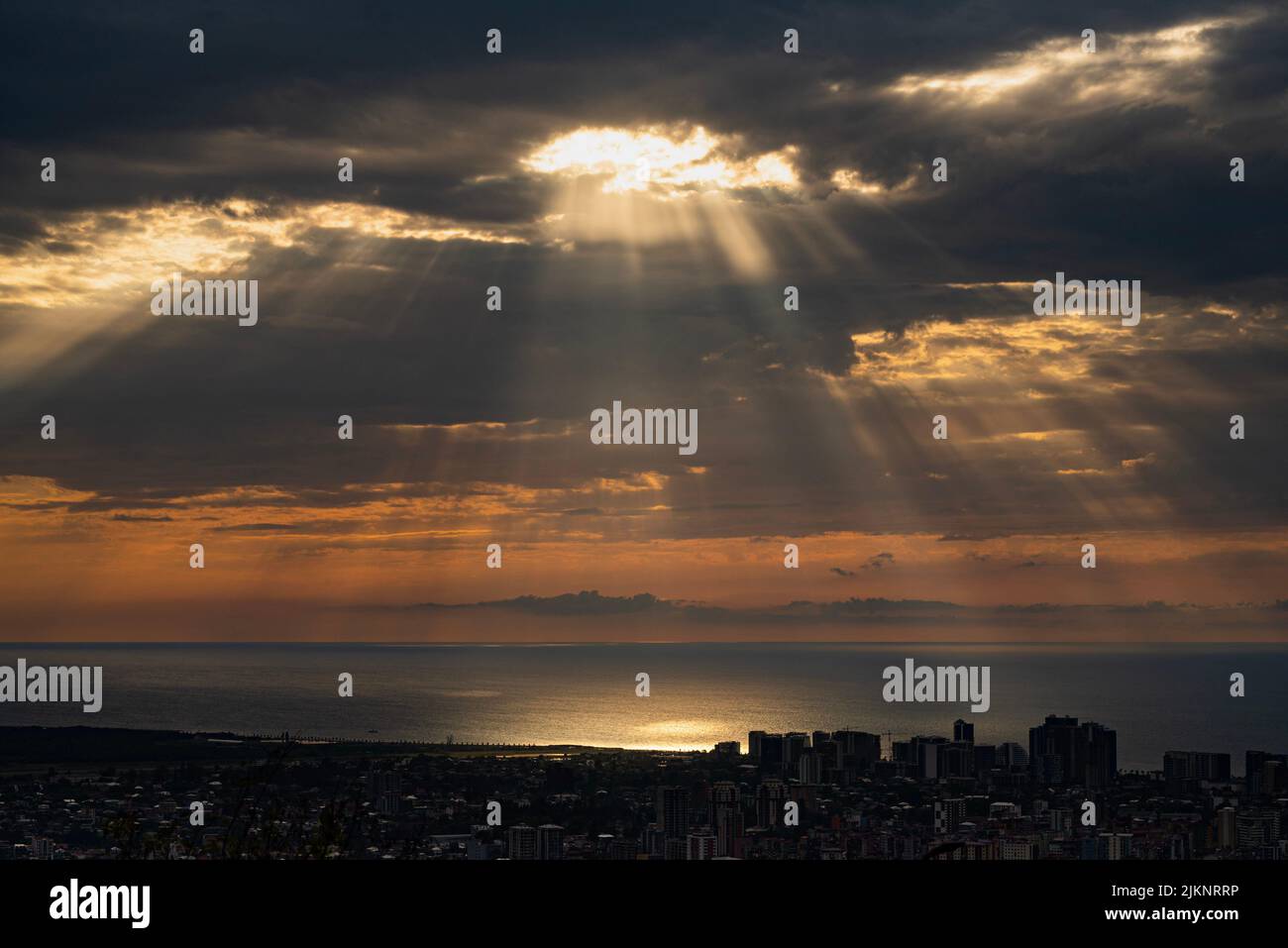 A scenic view of sun rays passing through dark clouds over a coastal ...