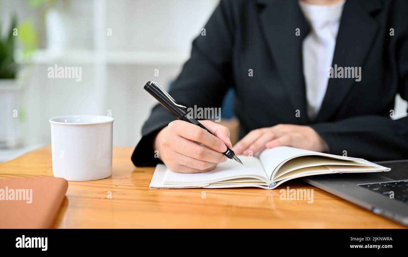 A businesswoman or female lawyer in formal black suit writing something ...