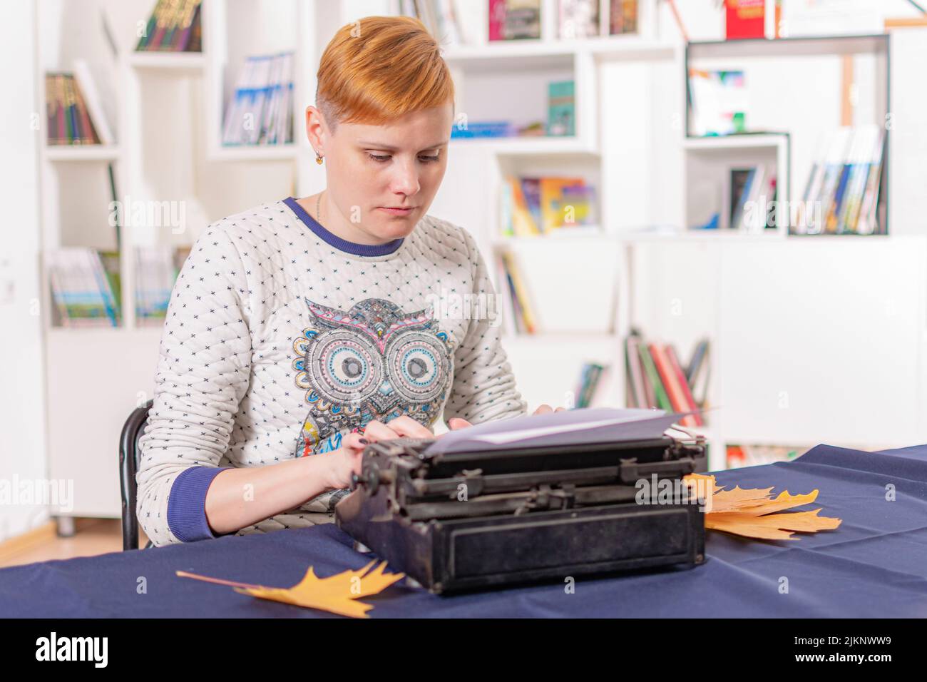 Serious young girl with red hair and stylish hairstyle sits at table ...