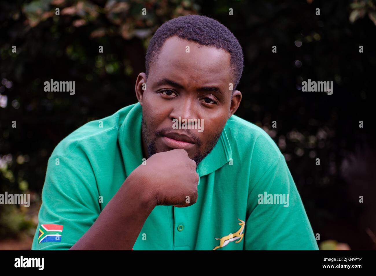 A sitting adult black man in green t-shirt with zimbabwe flag looking ...