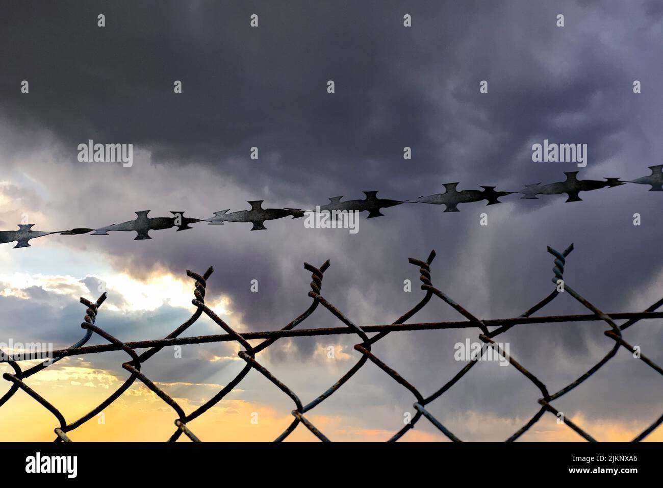 A low angle shot of barbed wire over a fence at sunset Stock Photo - Alamy