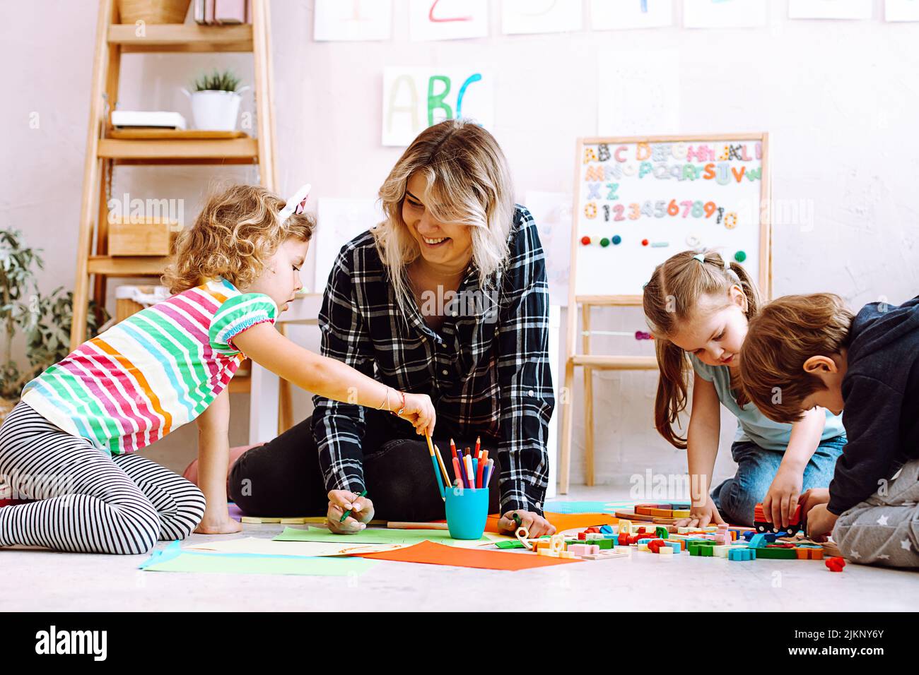 Portrait of young joyful woman teacher sit with children, looking at ...