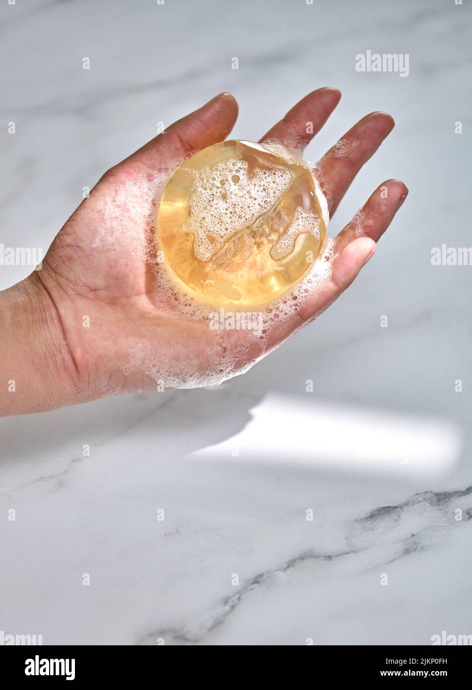 A vertical closeup shot of round glycerine soap in a hand with a foam ...