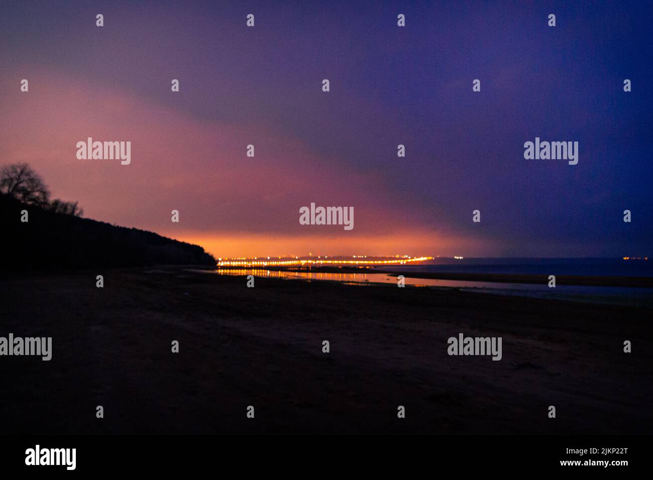A scenic night view of a body of water and the shore with city lights ...