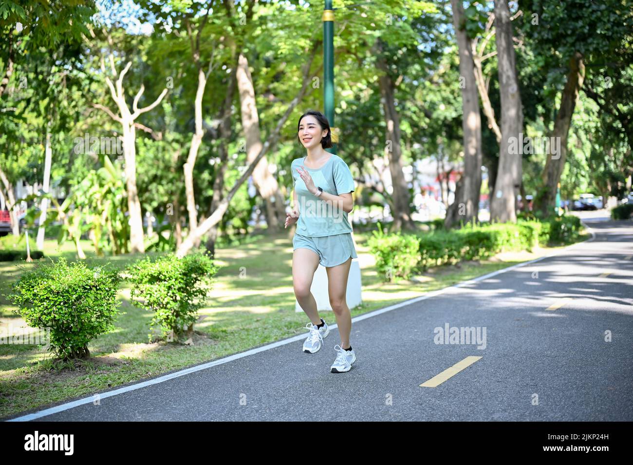 Active young Asian female runner in sportswear running at the beautiful ...