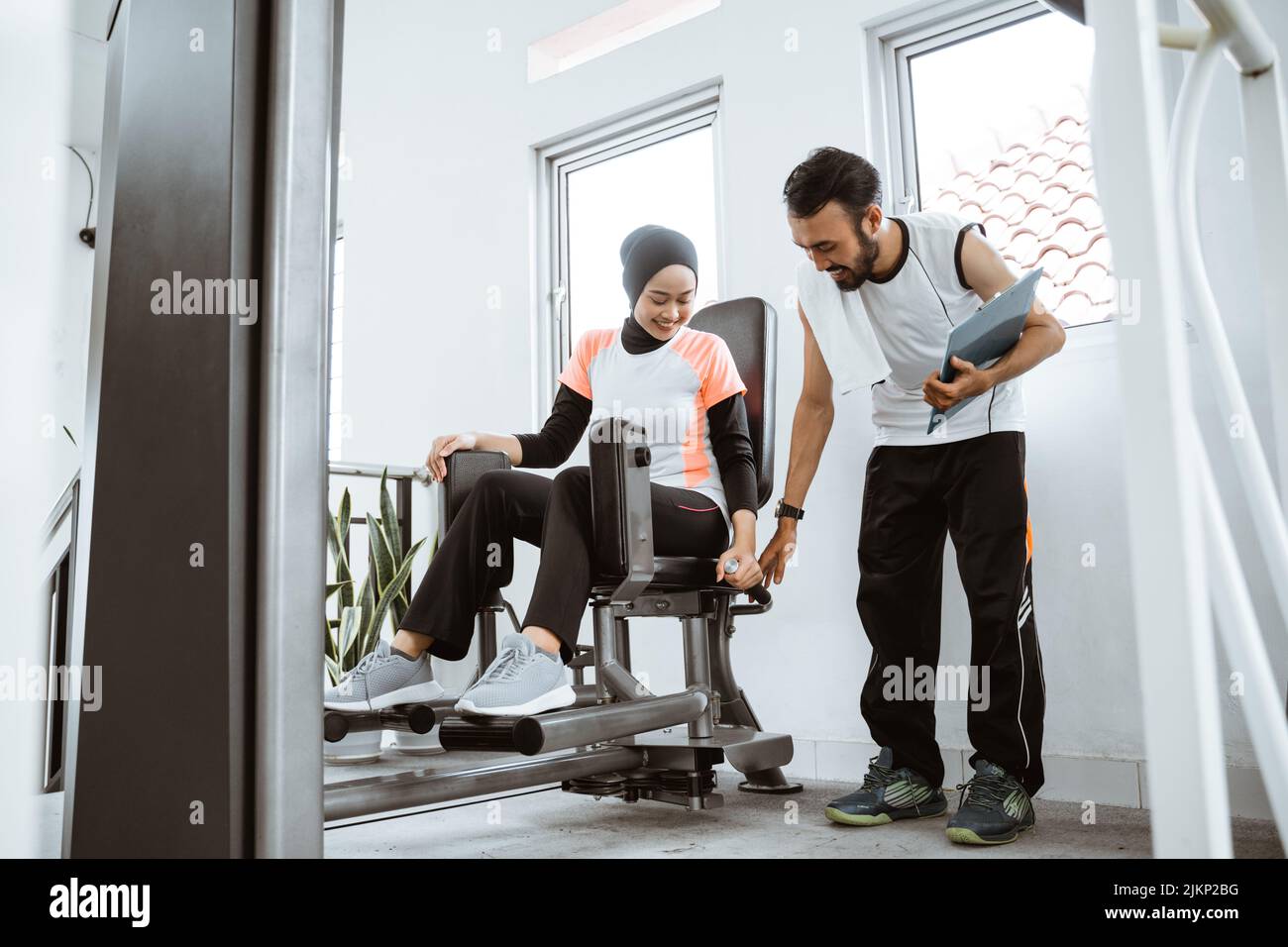 Personal trainer helping woman working with leg weight machine at the ...