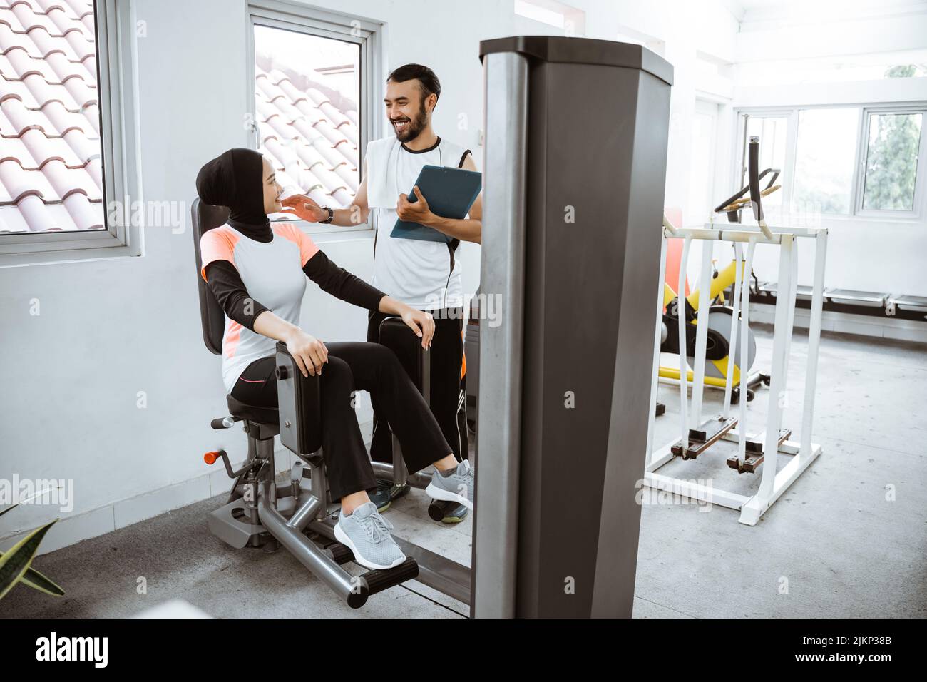 Personal trainer helping woman working with leg weight machine at the ...