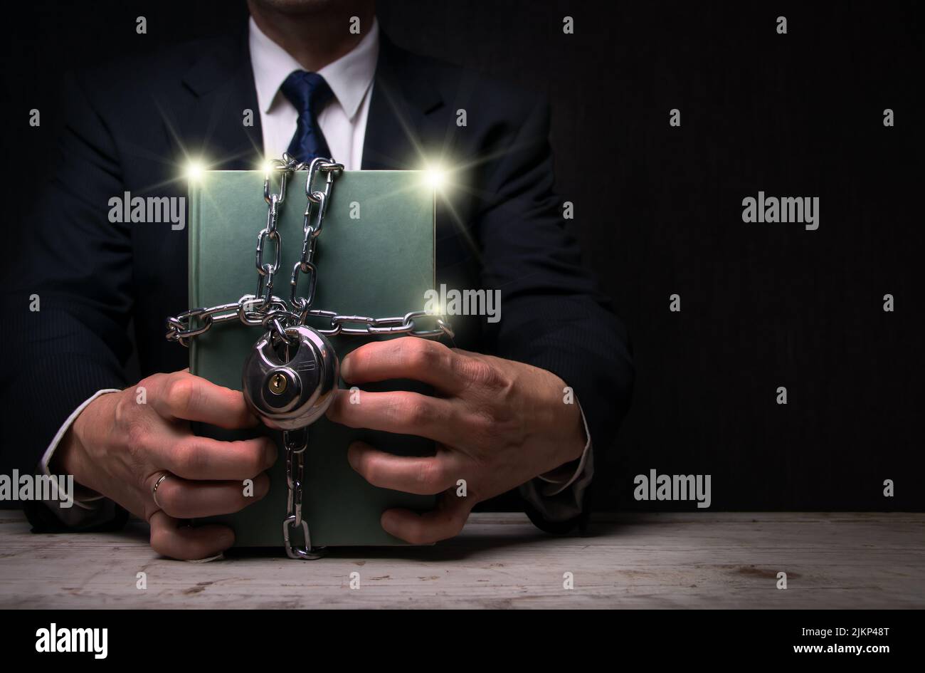 A businessman wearing a suit holding a book wrapped in chain and lock ...