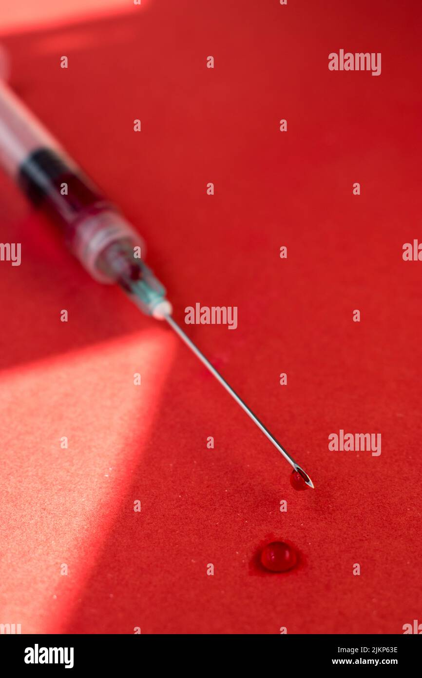 A vertical shot of a syringe with blood in it on a red surface. Blood ...