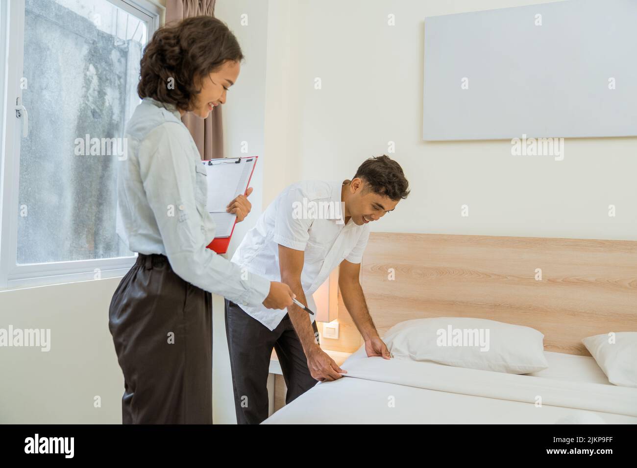 Female housekeeper carrying clipboard notes while supervising maid ...
