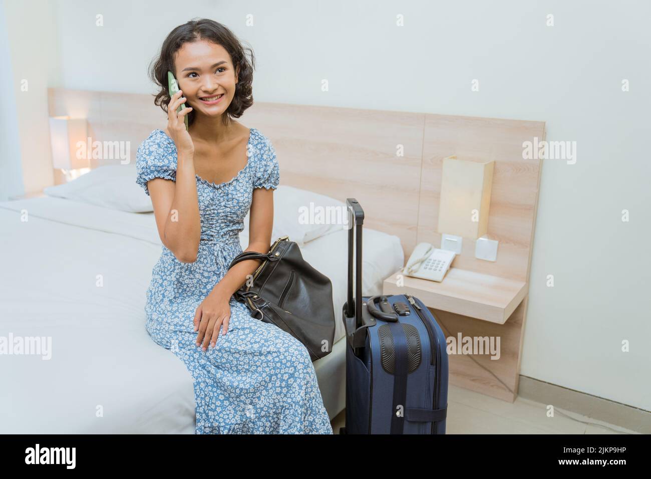 Female guest sitting on bed while calling using smartphone Stock Photo ...