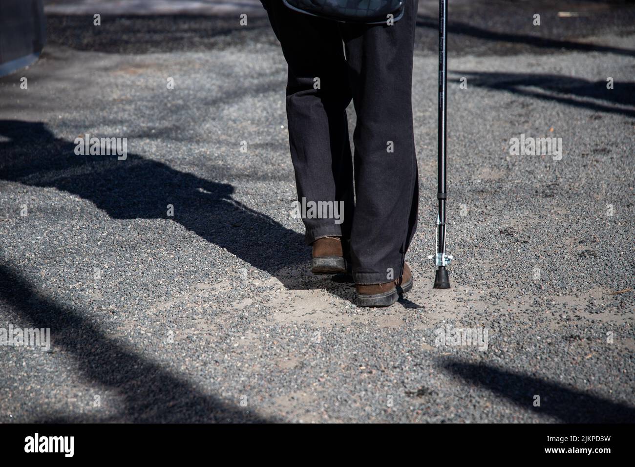 An elderly man on the street with a cane, a shadow on the street ...