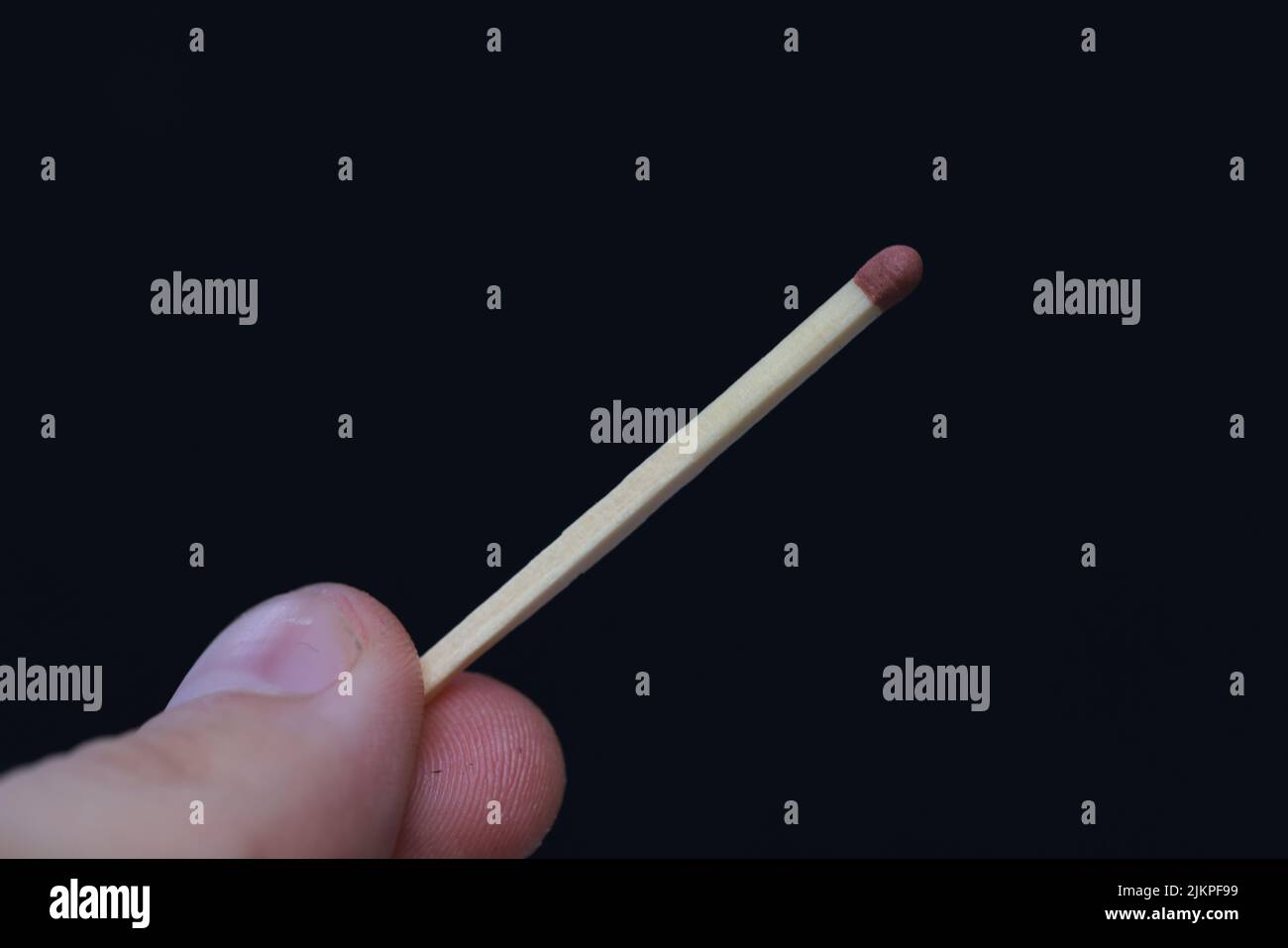 A closeup of a hand holding a match stick on a black background with ...