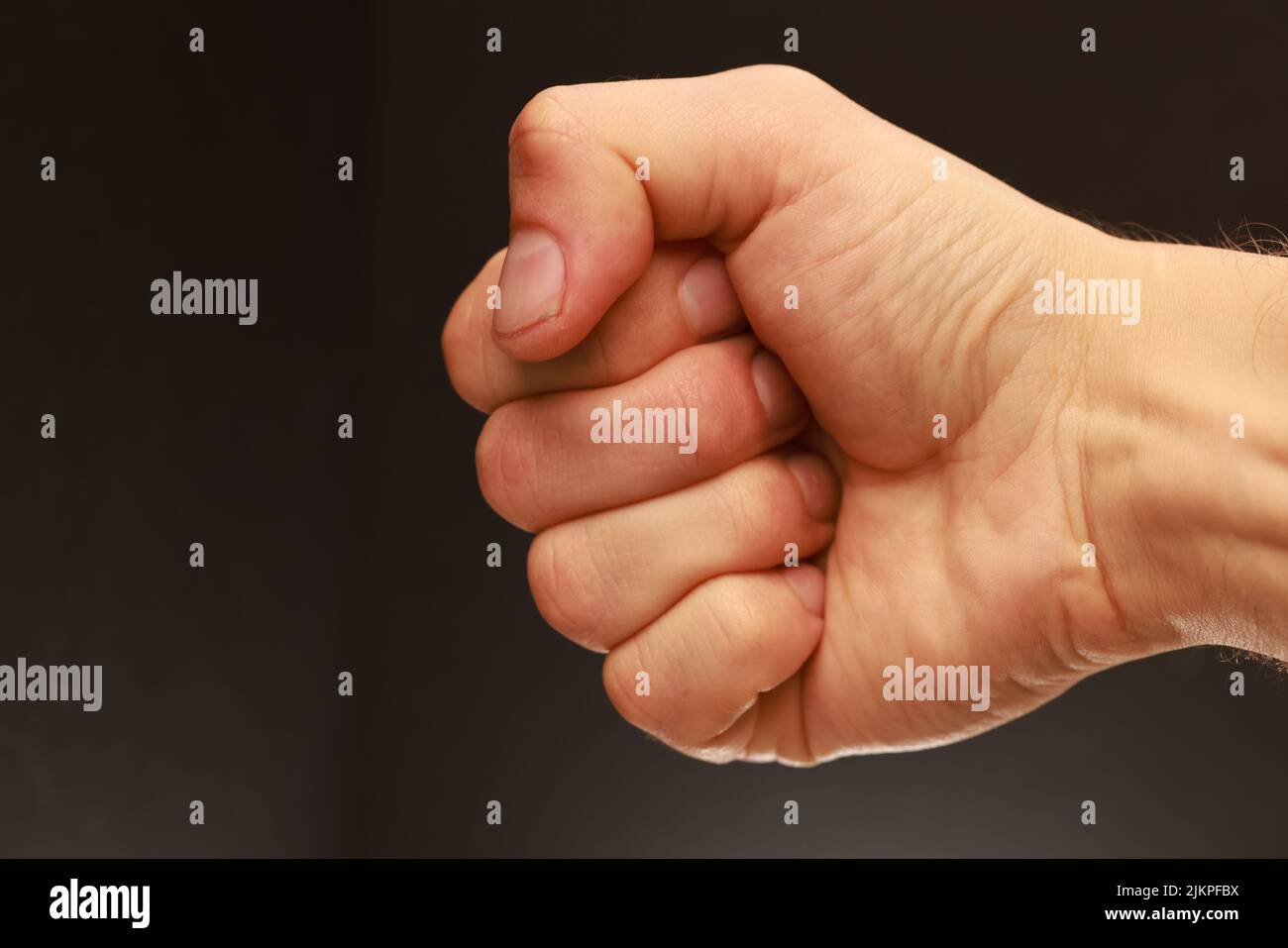 A closeup of the fist of a hand isolated on a brown blurry background ...