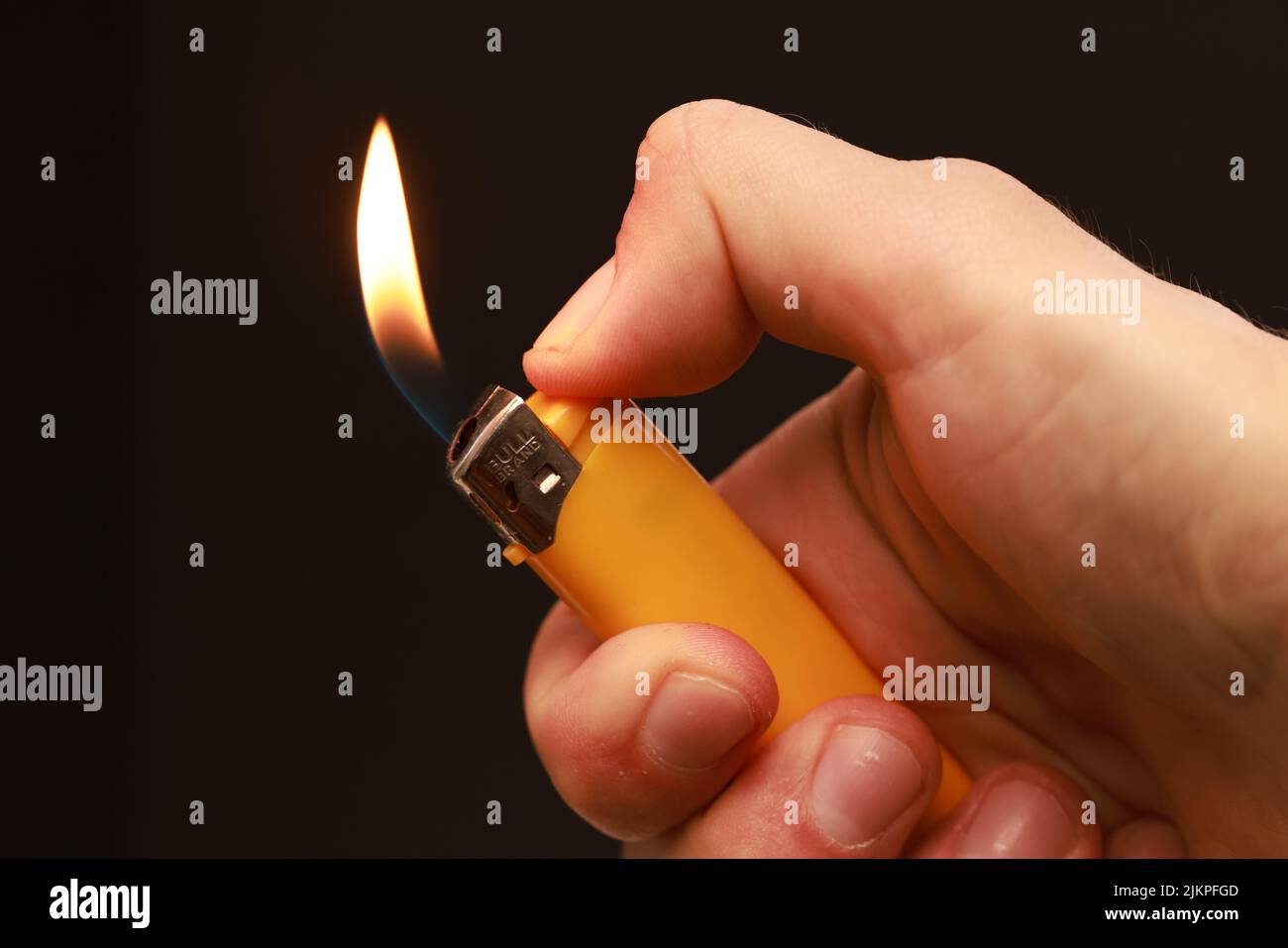 A closeup of a hand holding a burning cigarette lighter on a black ...