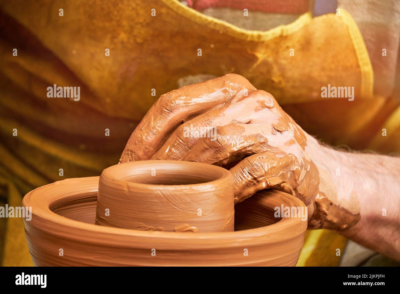 A man in old medieval Byzantine clothes sits behind a vintage potter's ...