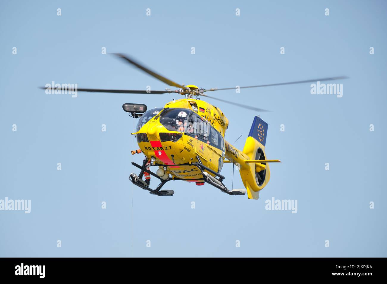 Yellow ADAC rescue helicopter hovering in the air, front view. German ...