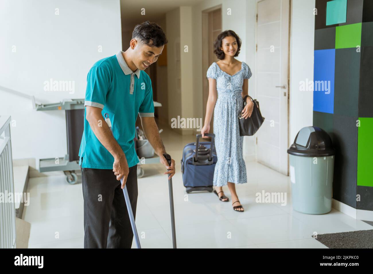 Janitor wearing turquoise uniform sweeps as female guests walk past Stock Photo - Alamy