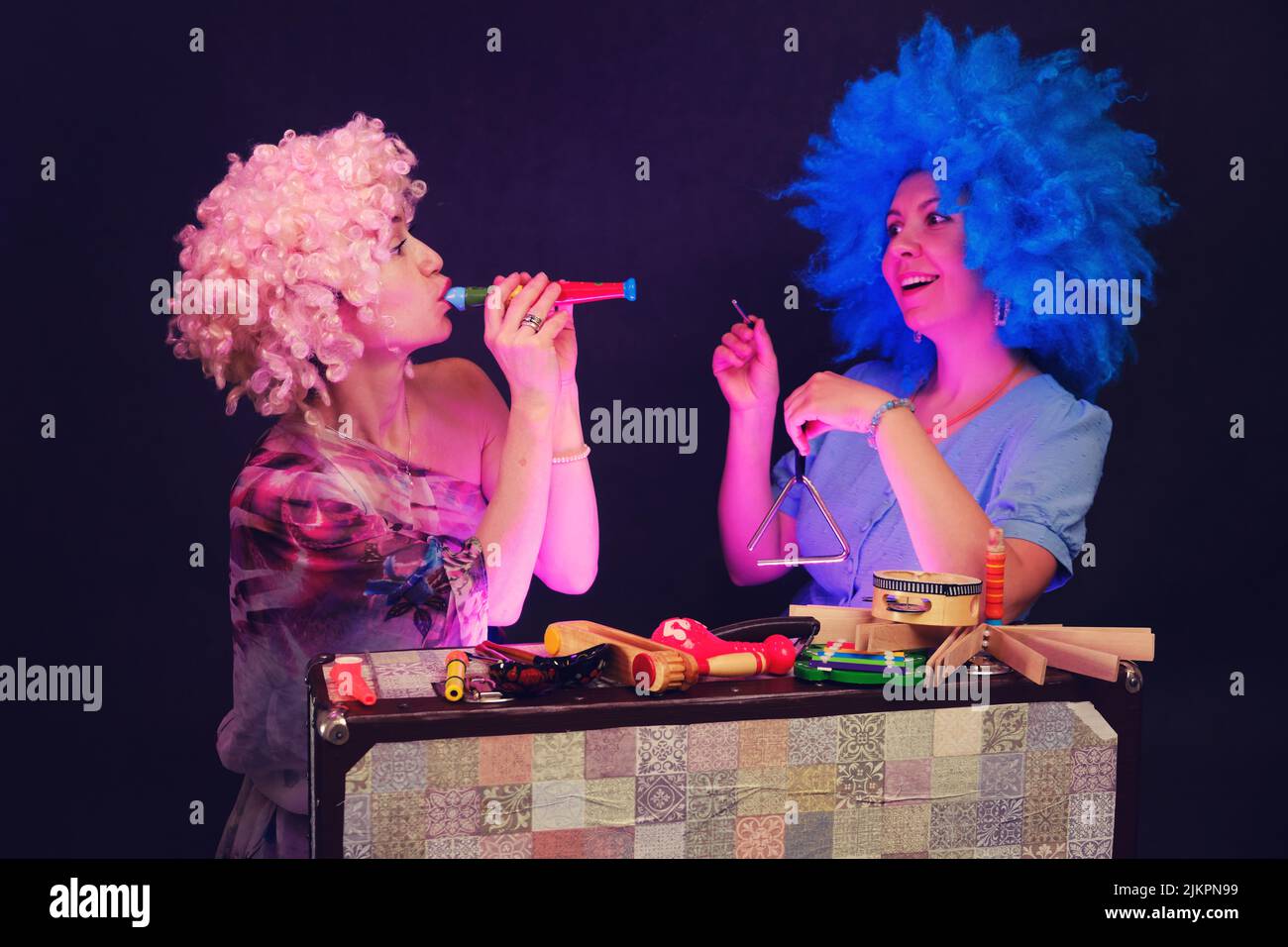 Happy women in funny wigs give a musical performance on a studio black ...