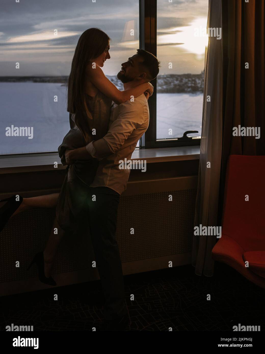 Happy loving couple in hotel standing on window background on sunset ...