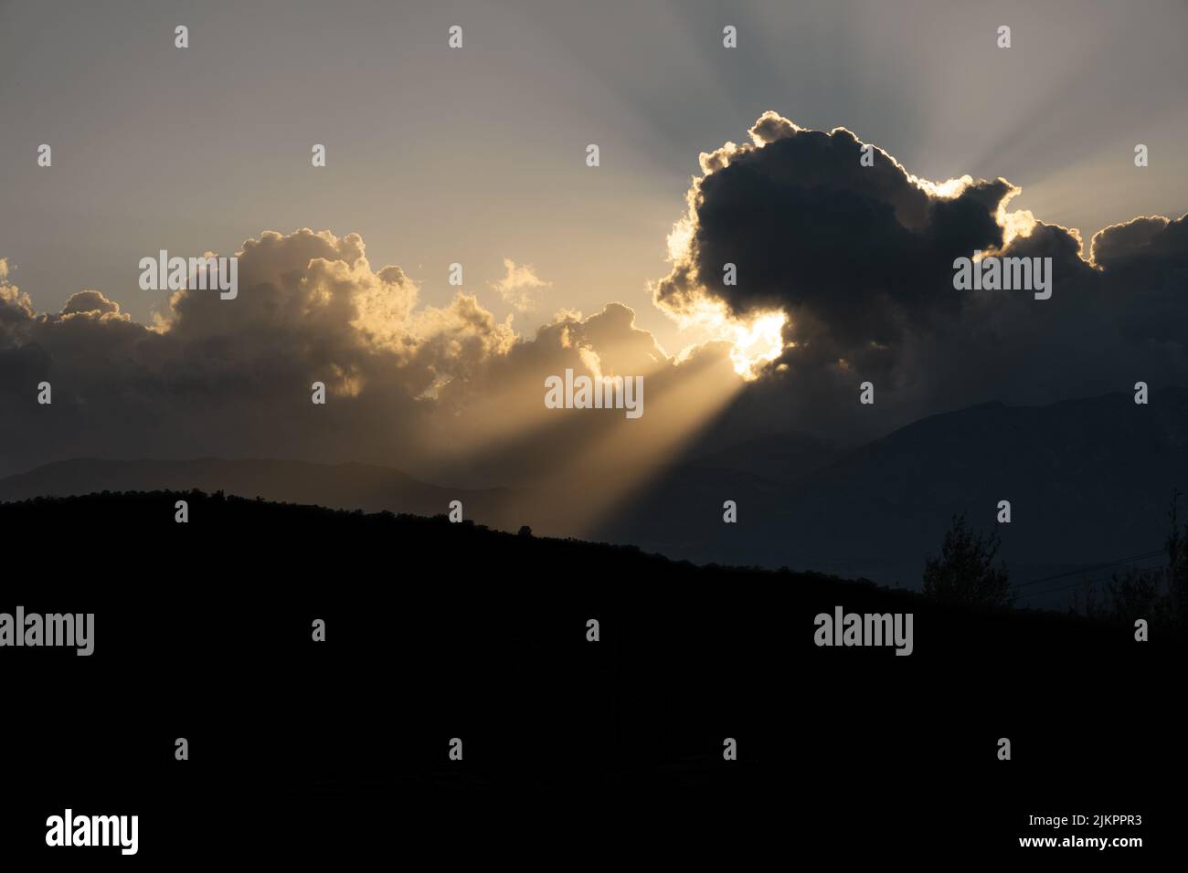 A view of sun rays through clouds and sunset behind mountains Stock Photo - Alamy